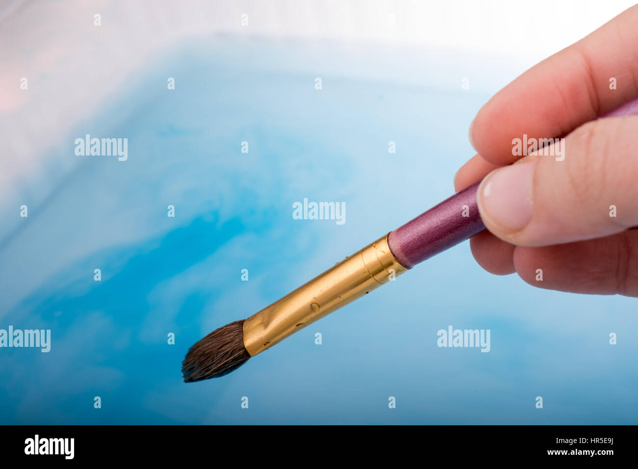 Watercolor paint dissolving in water as painting brush touches water ...