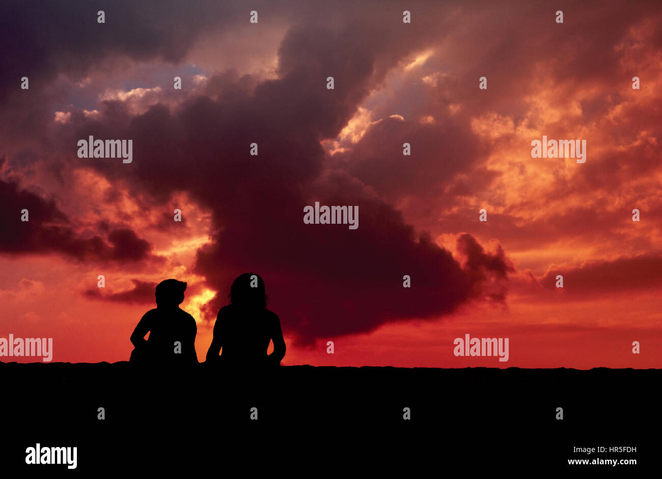 silhouettes of a couple of women sitting on the ground observing the ...