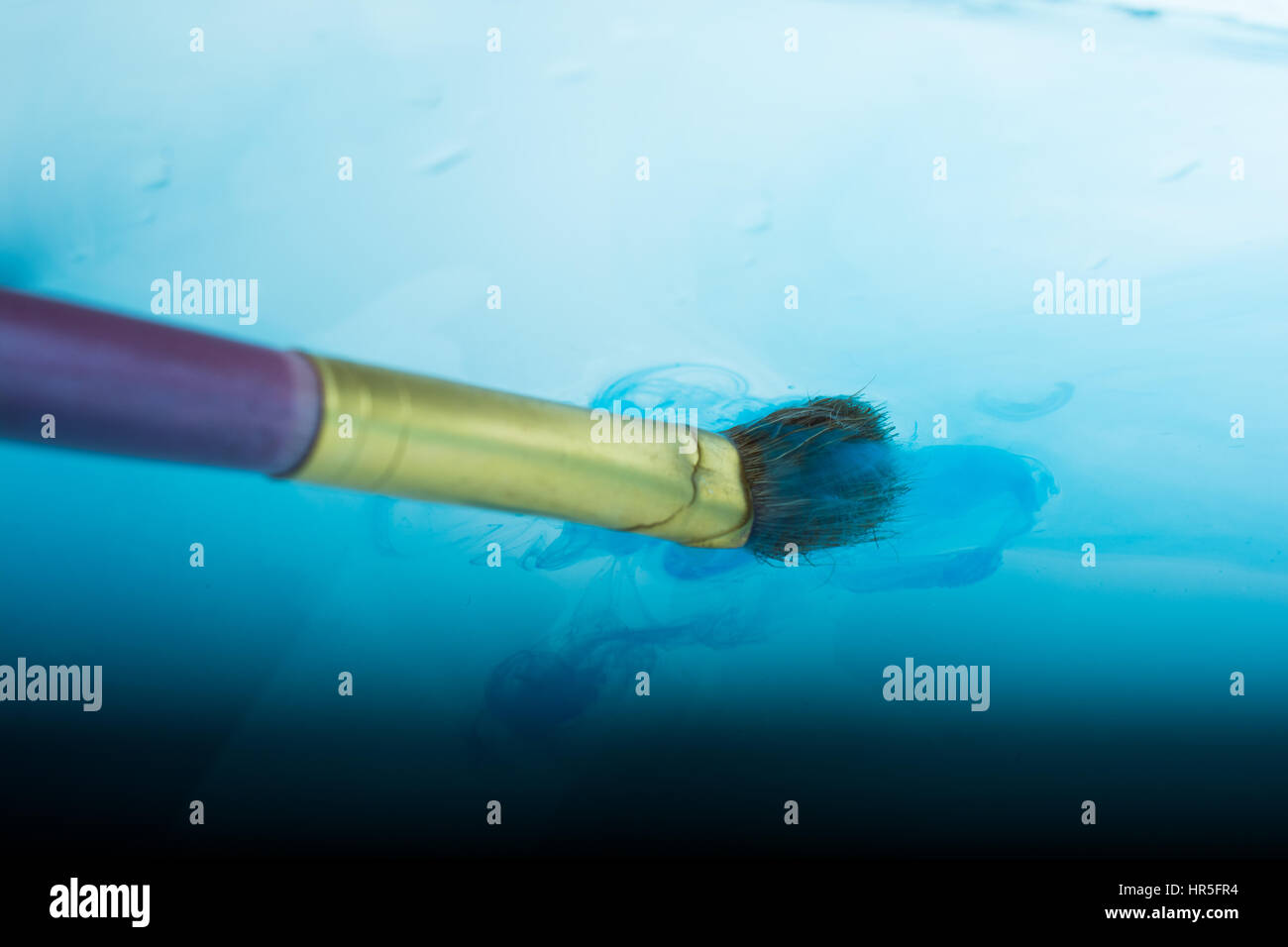 Watercolor paint dissolving in water as painting brush touches water ...