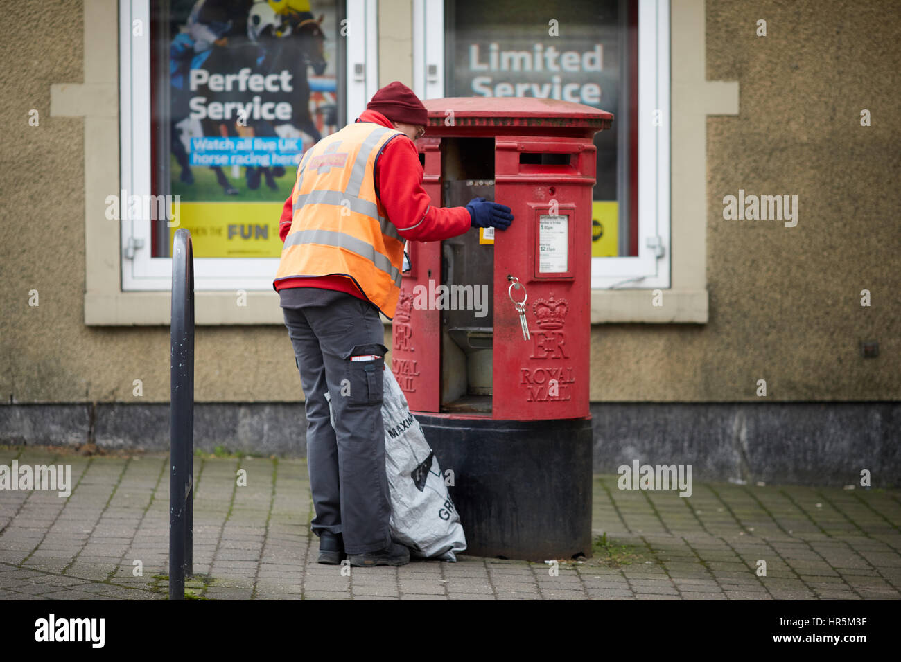 Postman in uniform emptying letters from a red Royal Mail postbox at ...
