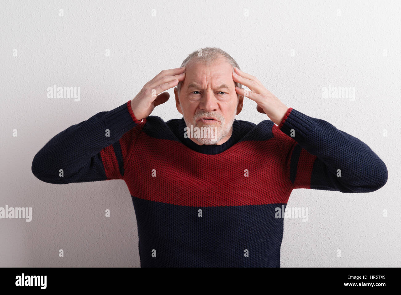 Angry senior man in red and blue sweater holding head. Studio shot ...