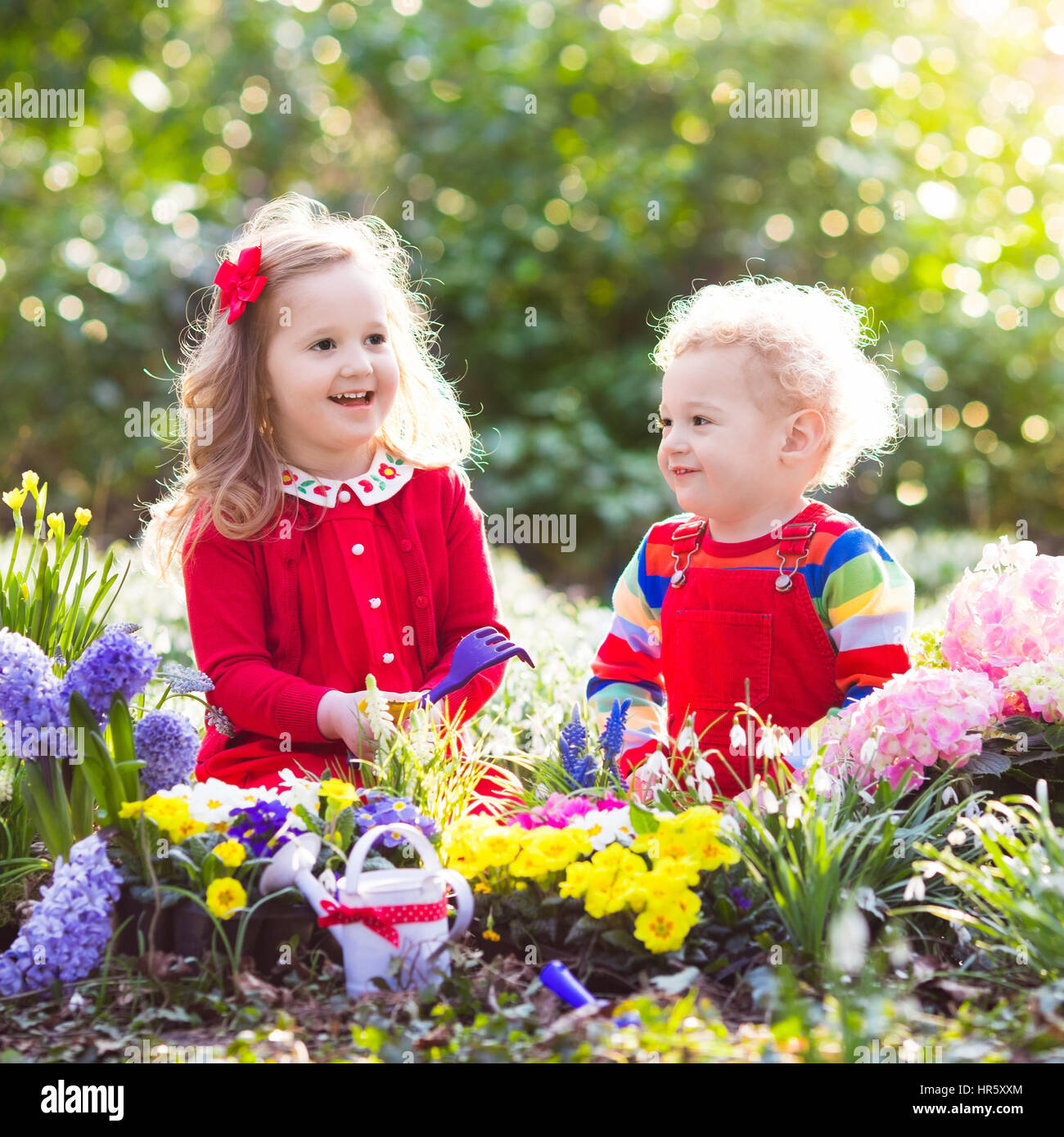 Children planting spring flowers in sunny garden. Little boy and girl ...