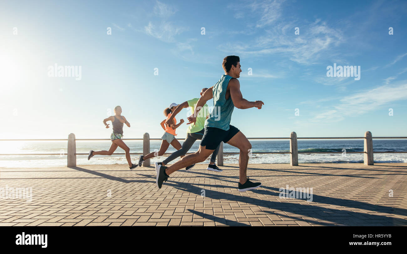 Portrait of young runners sprinting on the ocean front path. Group ...