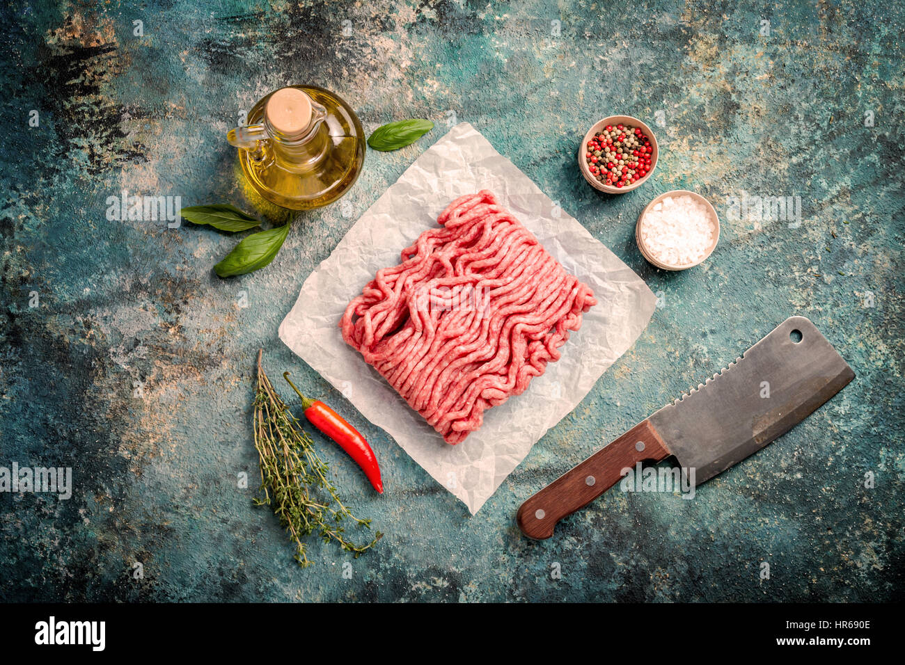 Raw minced meat with olive oil and seasoning on paper over blue stone ...