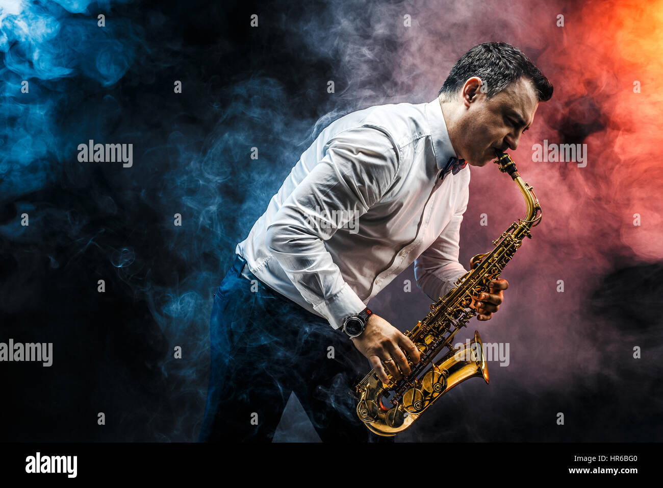 Side view of elegant handsome man playing saxophone in studio against ...