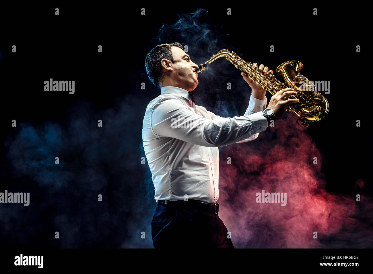 Side view of elegant handsome man playing saxophone in studio against ...