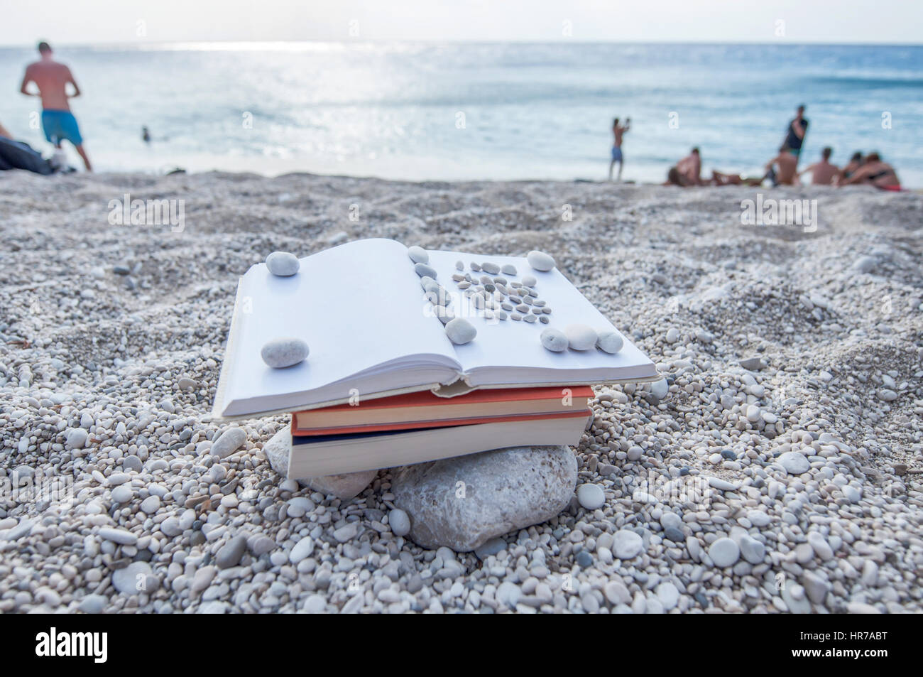Open book at beach on a pile of books near the sea during summer sunset ...