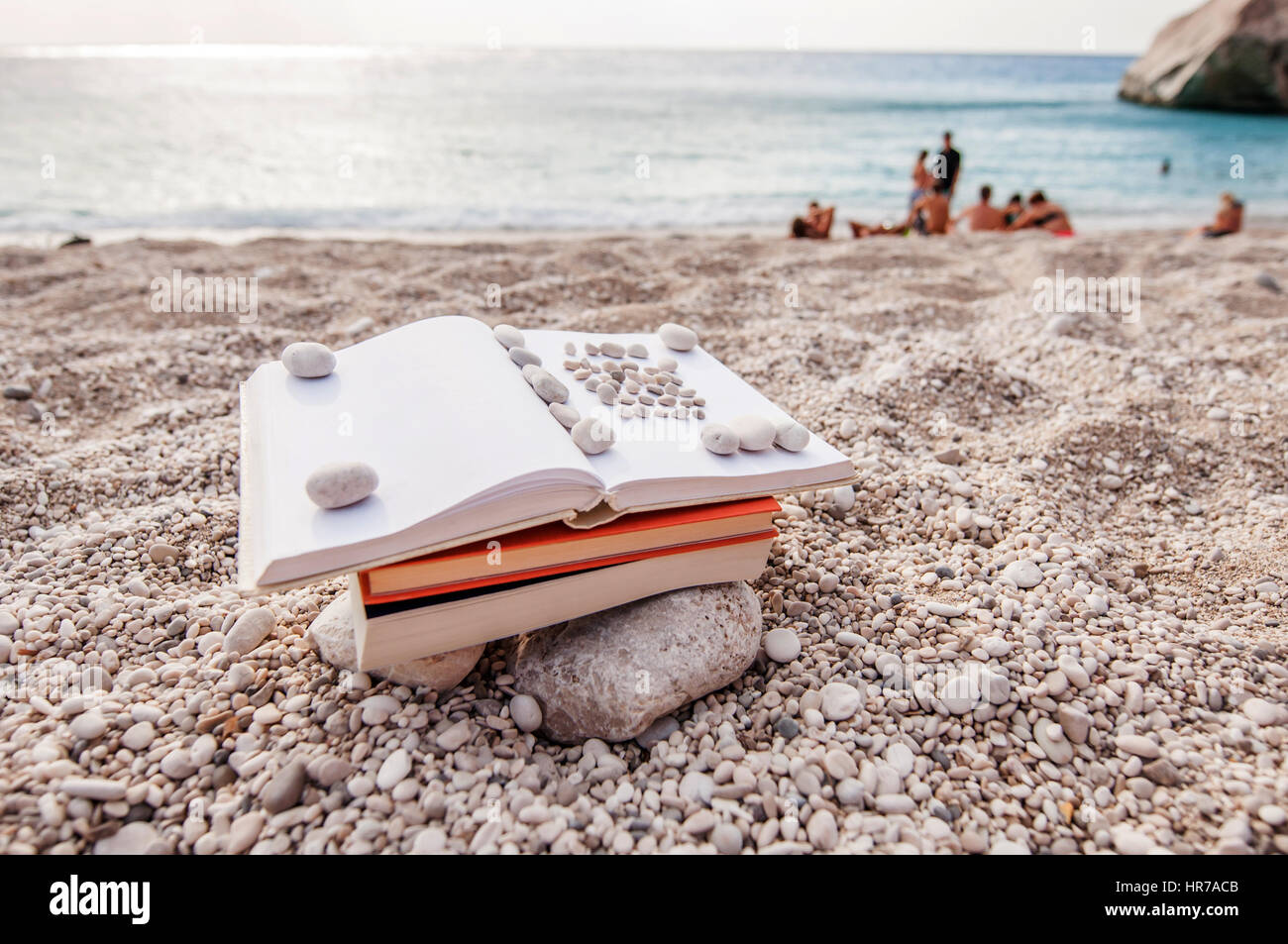Open book at beach on a pile of books near the sea during summer sunset ...