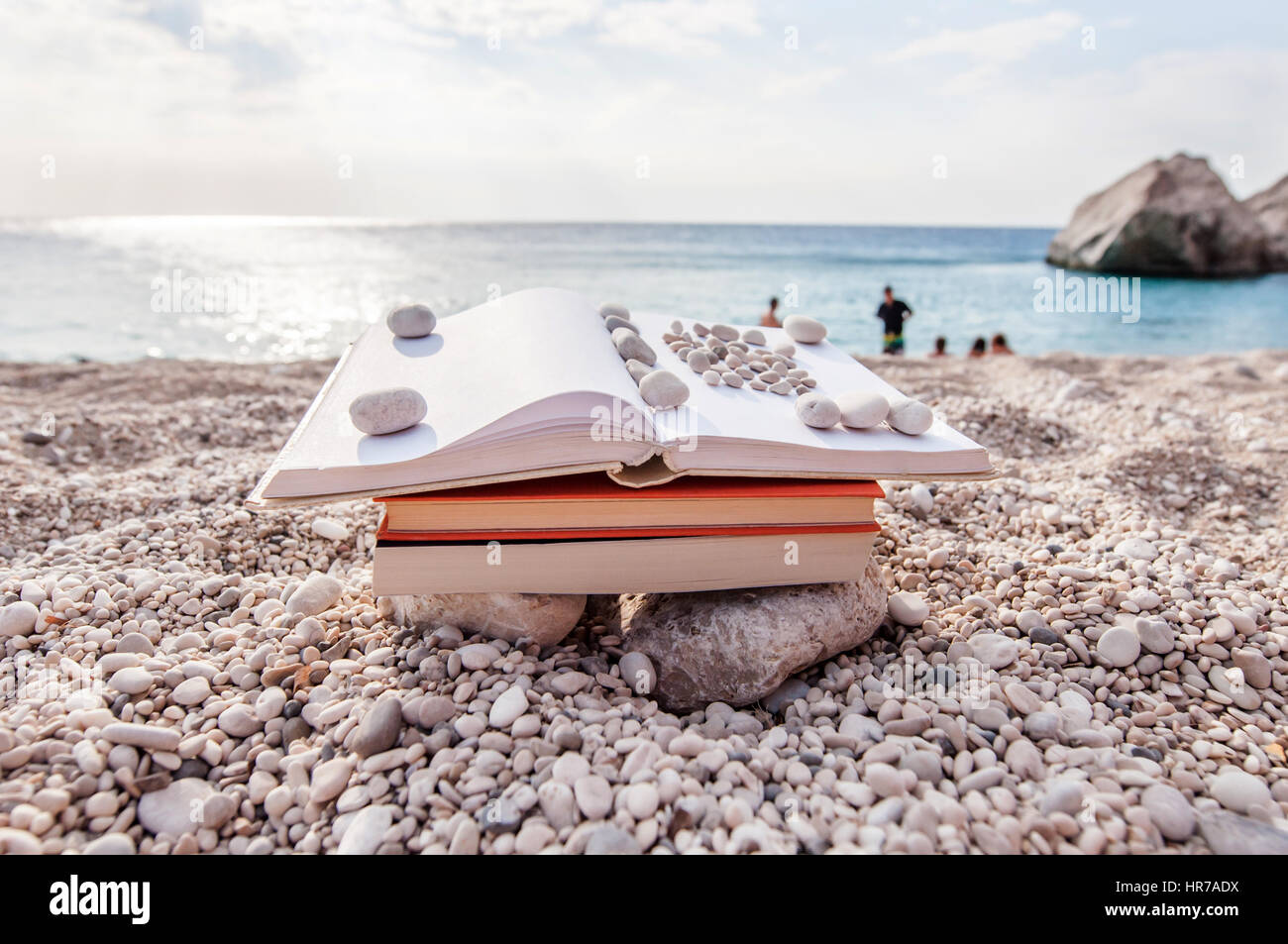 Open book at beach on a pile of books near the sea during summer sunset ...