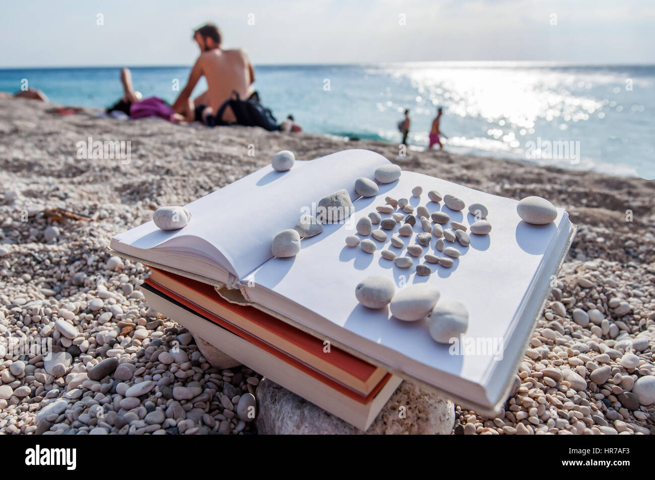 Open book at beach on a pile of books near the sea during summer sunset ...