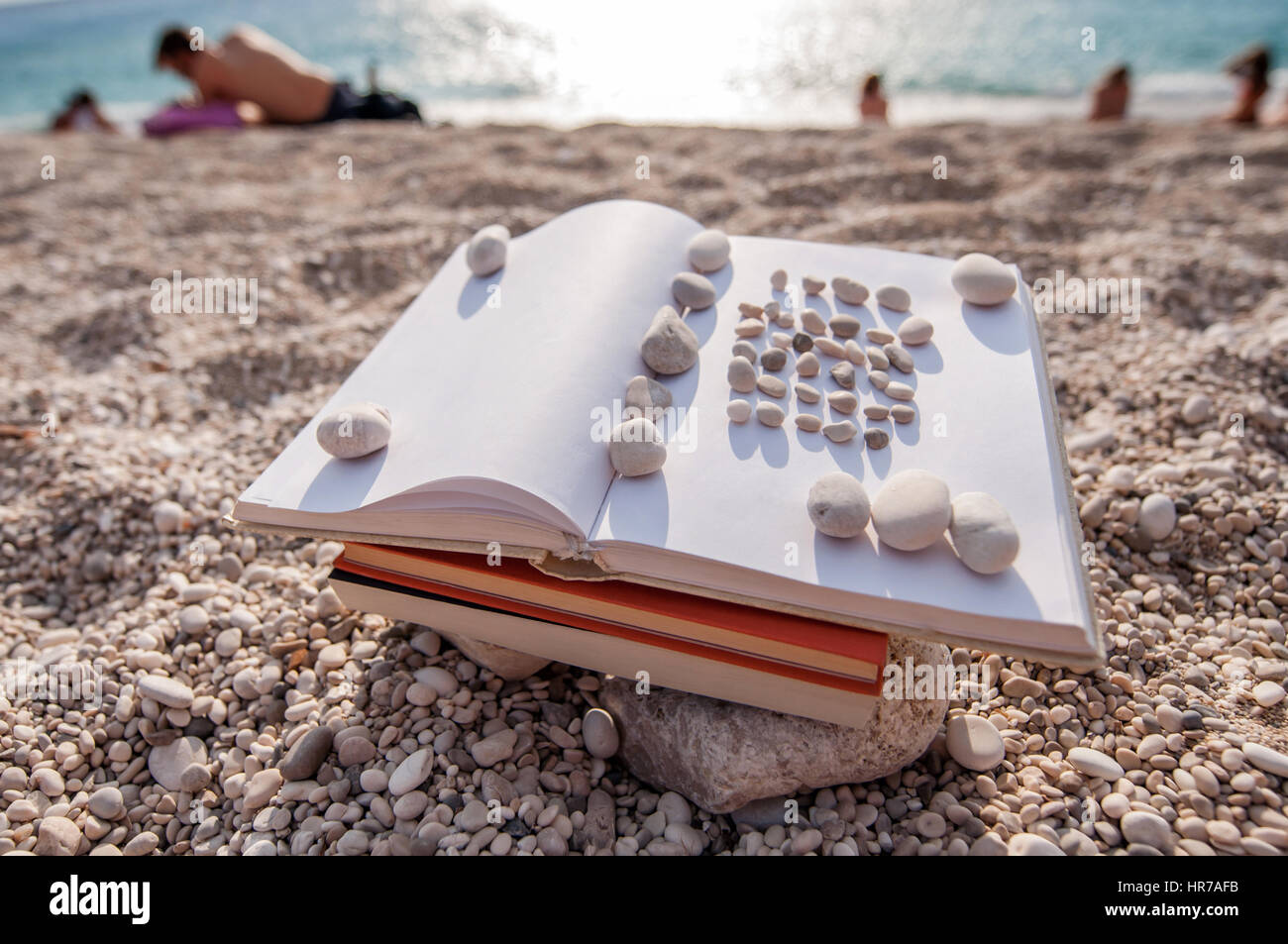 Open book at beach on a pile of books near the sea during summer sunset ...
