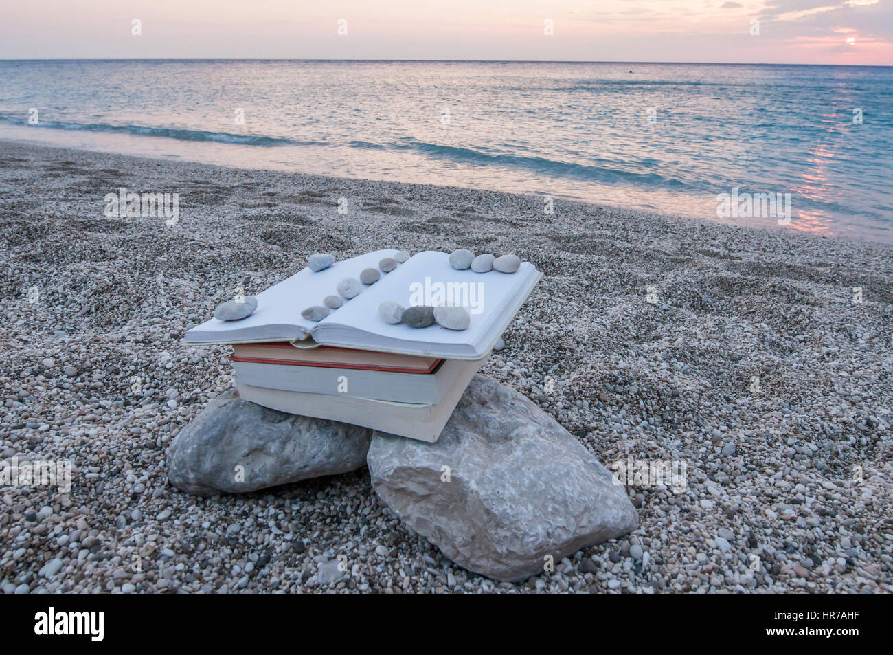 Open book at beach on a pile of books near the sea during summer sunset ...