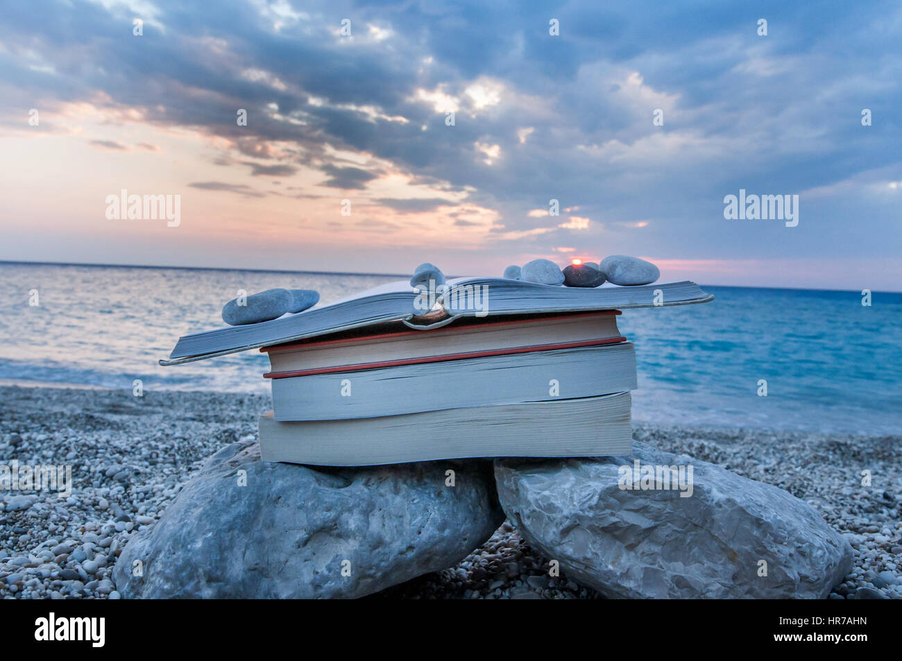 Open book at beach on a pile of books near the sea during summer sunset ...