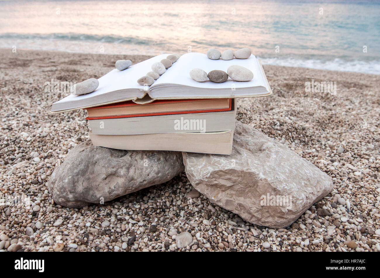 Open book at beach on a pile of books near the sea during summer sunset ...