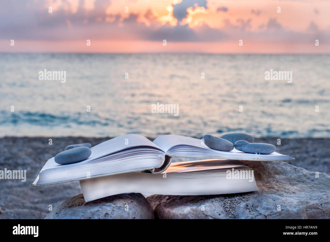 Open book at beach on a pile of books near the sea during summer sunset ...