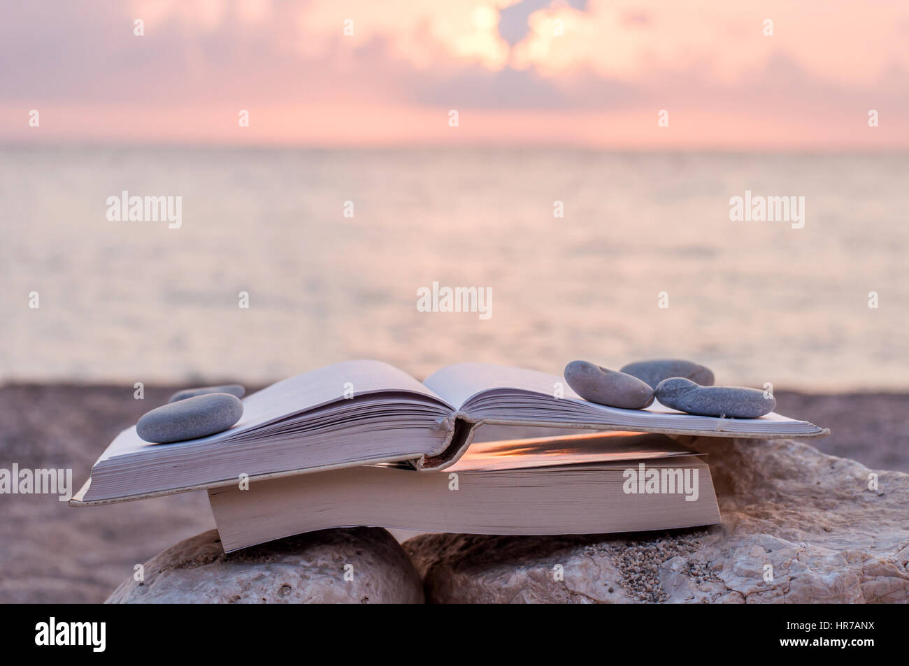 Open book at beach on a pile of books near the sea during summer sunset ...