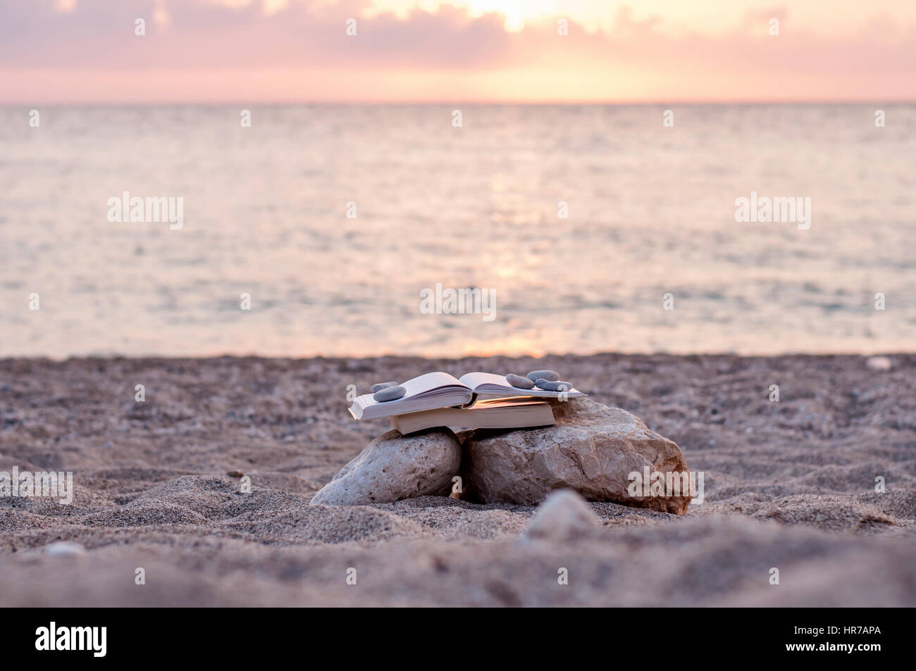 Open book at beach on a pile of books near the sea during summer sunset ...