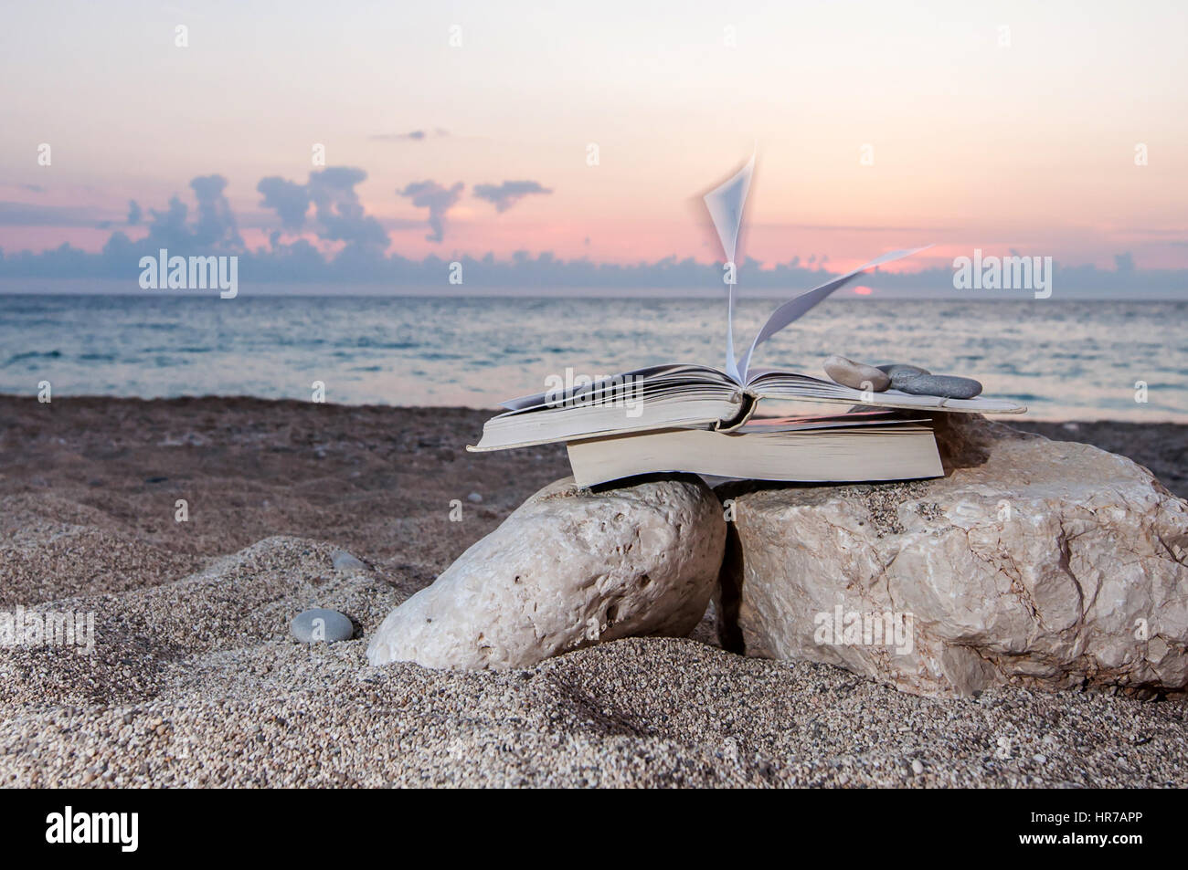 Open book at beach on a pile of books near the sea during summer sunset ...
