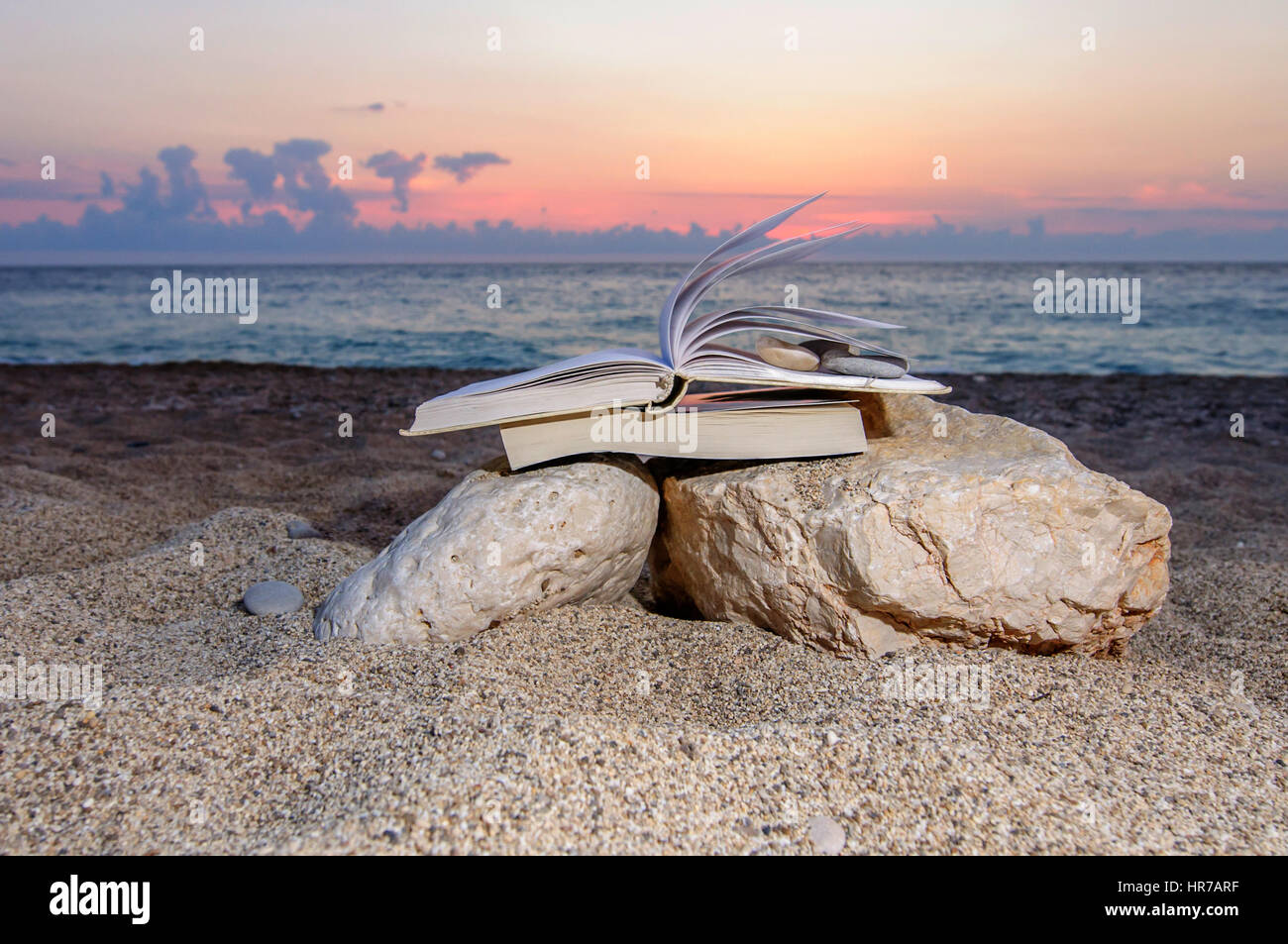 Open book at beach on a pile of books near the sea during summer sunset ...
