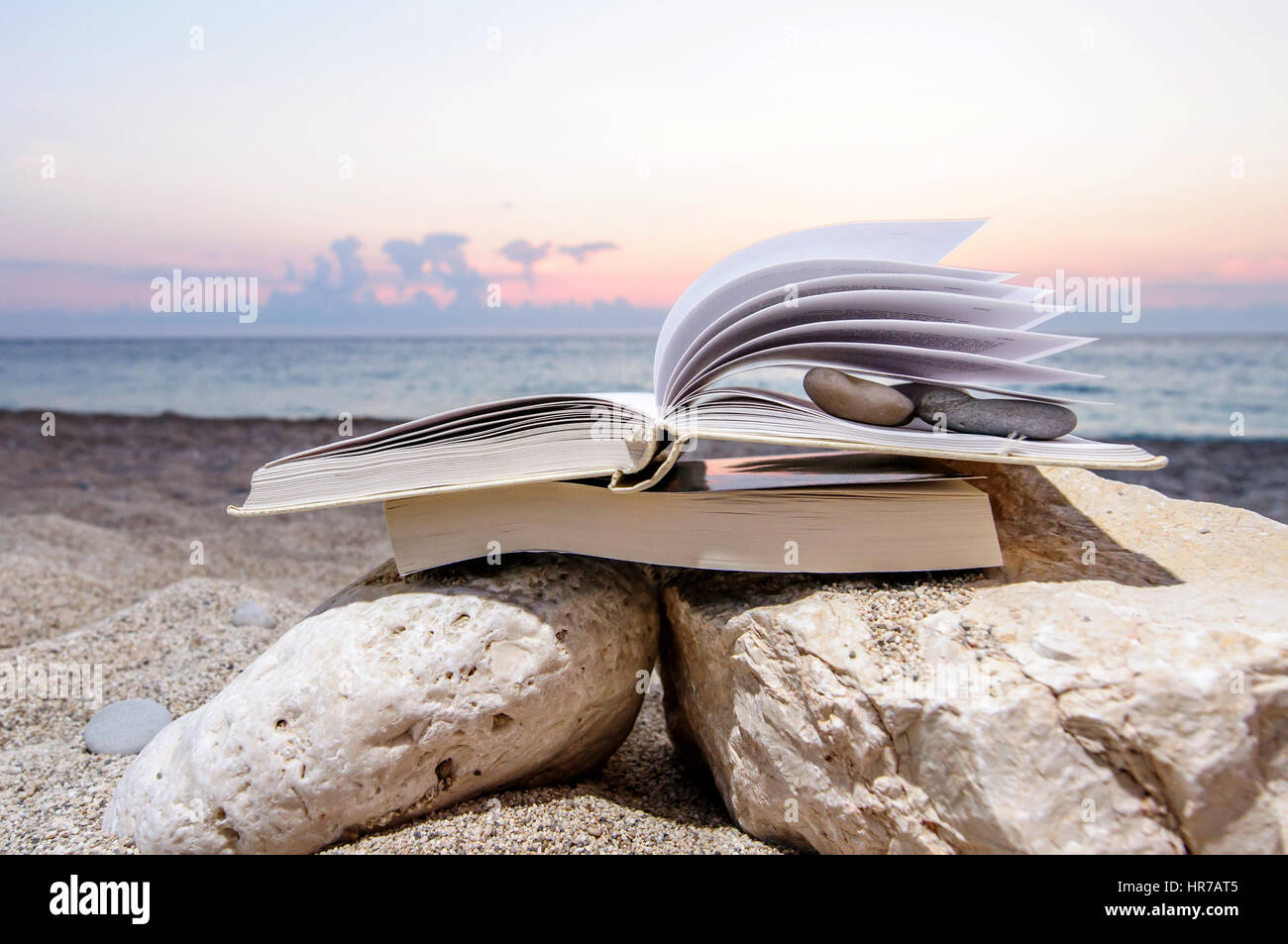 Open book at beach on a pile of books near the sea during summer sunset ...