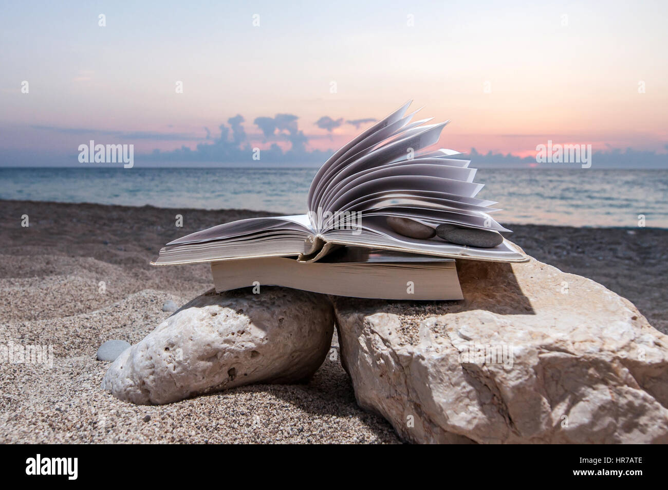 Open book at beach on a pile of books near the sea during summer sunset ...