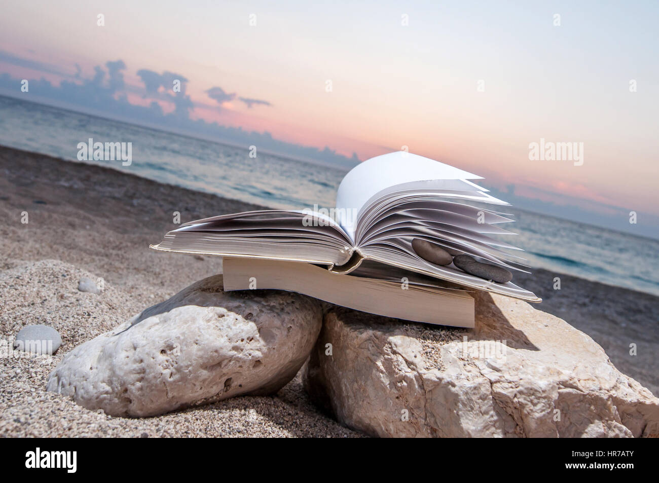 Open book at beach on a pile of books near the sea during summer sunset ...