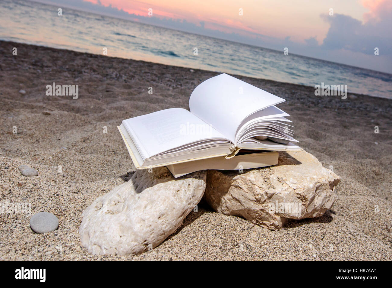 Open book at beach on a pile of books near the sea during summer sunset ...