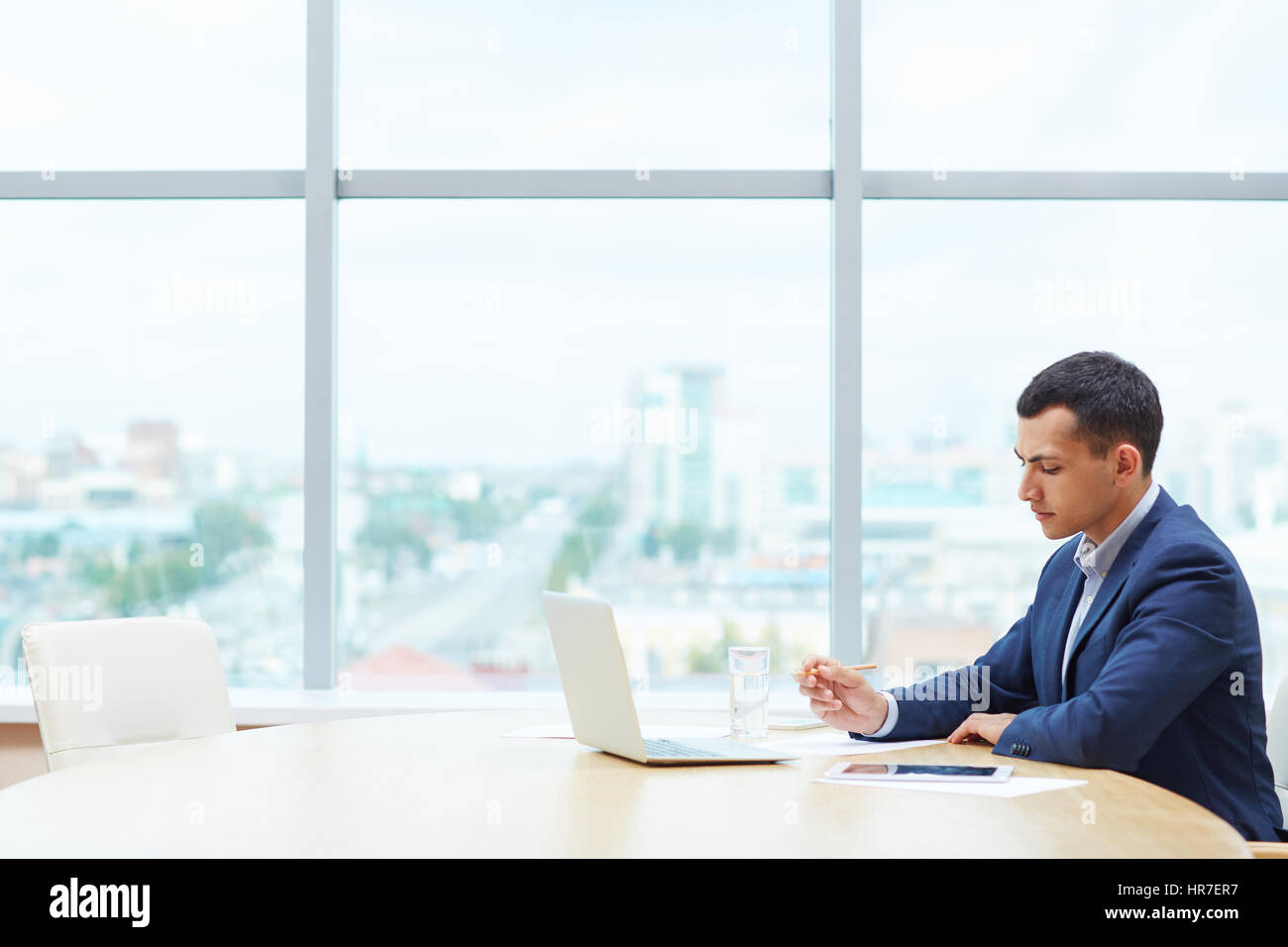 Profile view of young business man sitting alone against window at ...