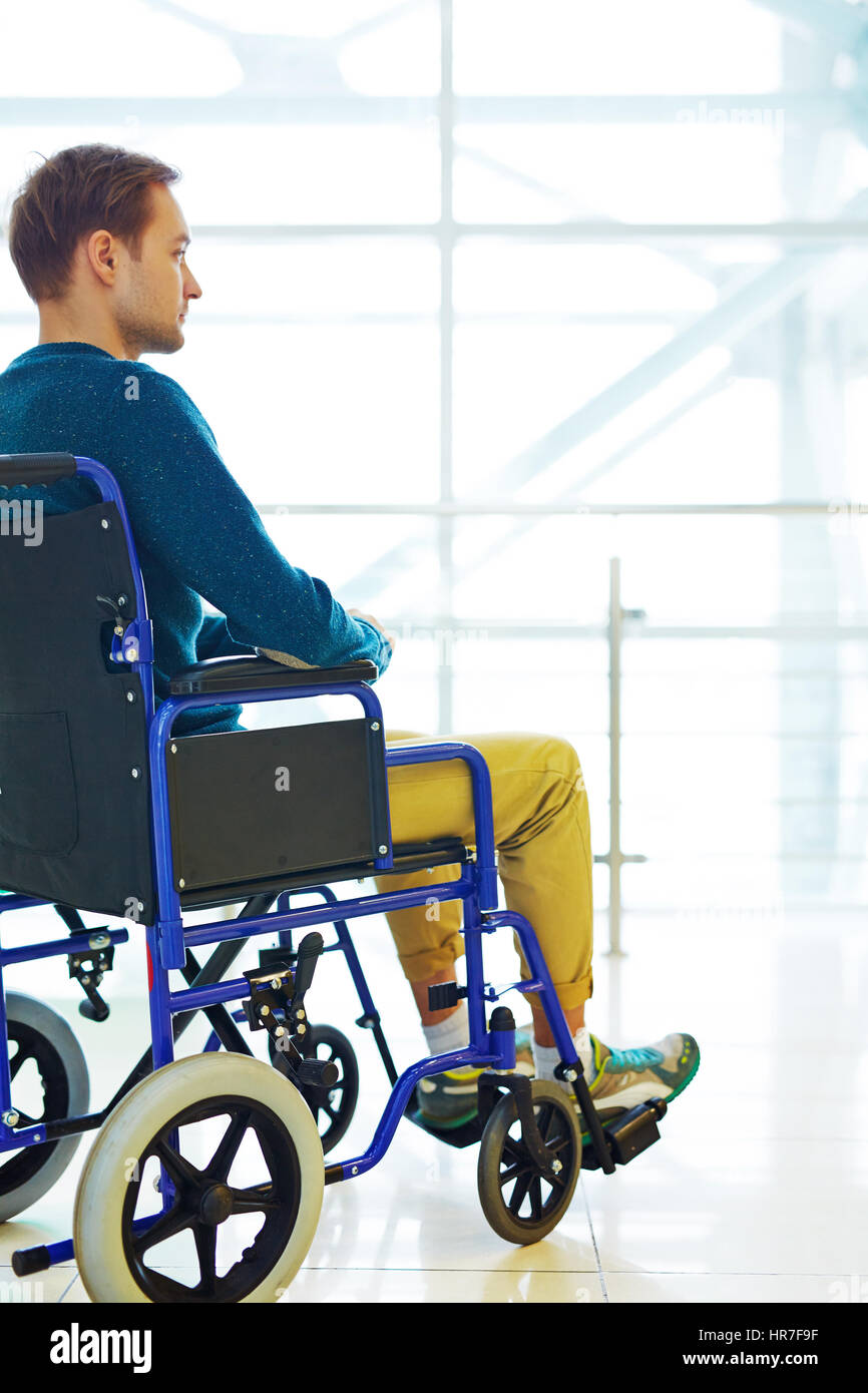 Side view of young man sitting in wheelchair and looking into the ...