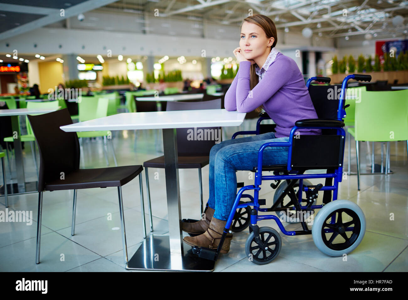 Young physically impaired girl sitting in wheelchair at mall food court ...