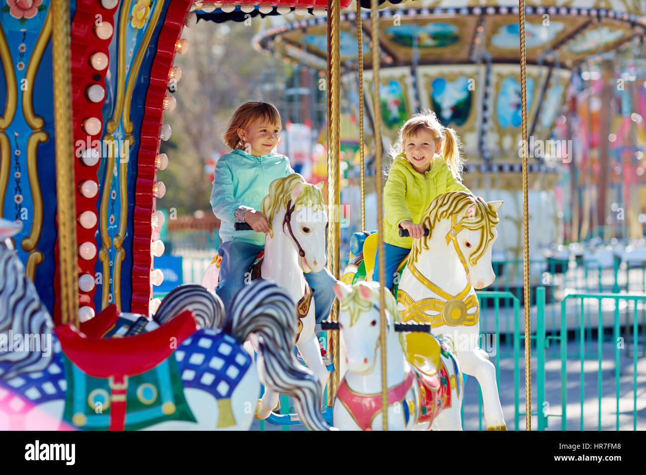 Cute little sisters enjoying spring in funfair: they riding on colorful ...