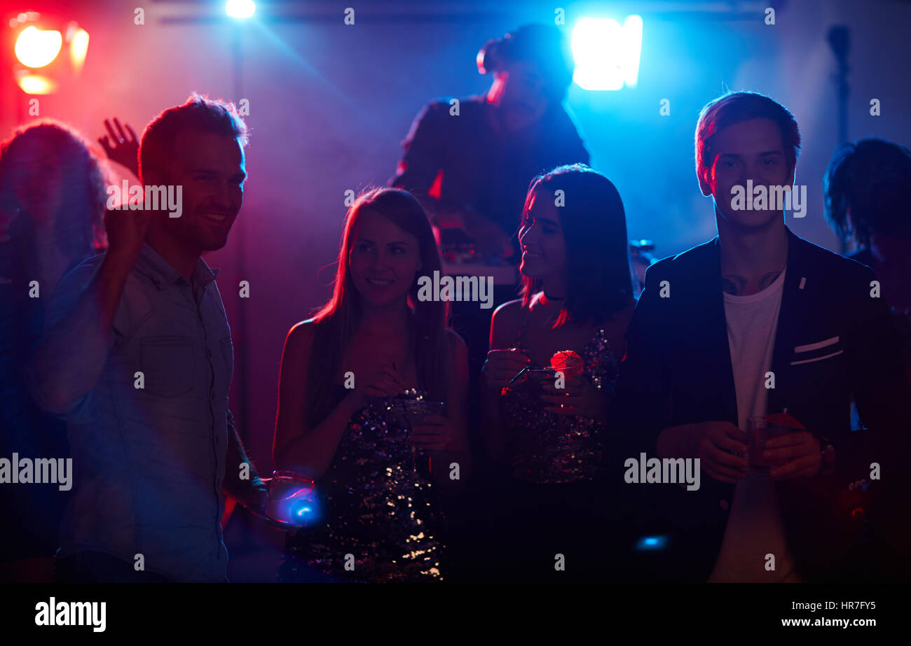 Group of dressed-up young people hanging out in night club, holding ...