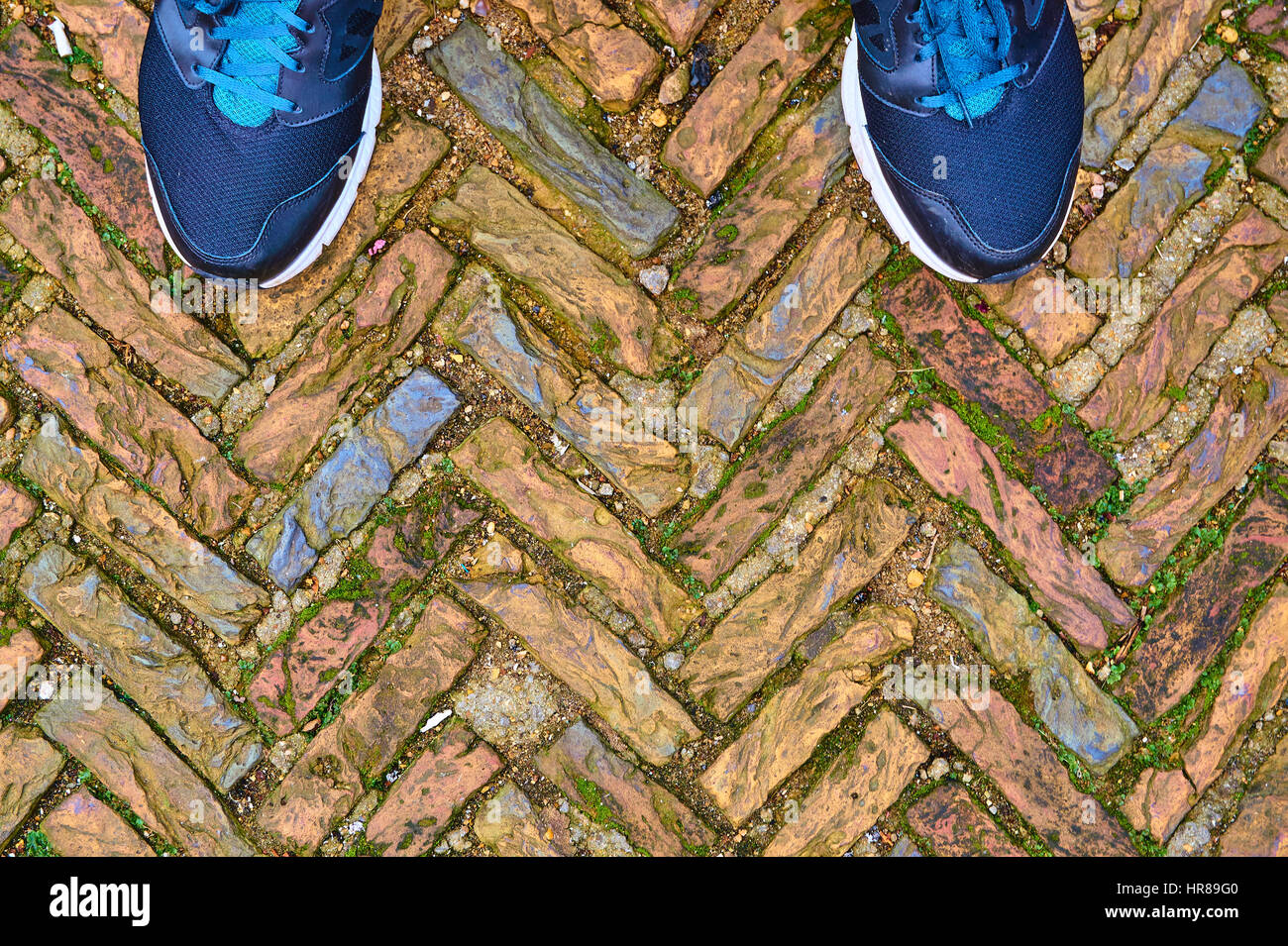 Old cobble stones in a herringbone pattern with toes of modern training ...