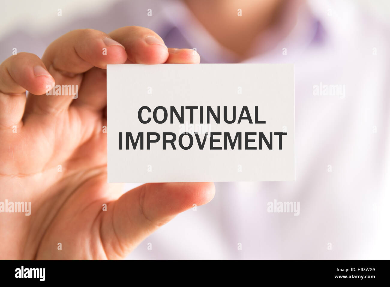 Closeup on businessman holding a card with CONTINUAL IMPROVEMENT ...