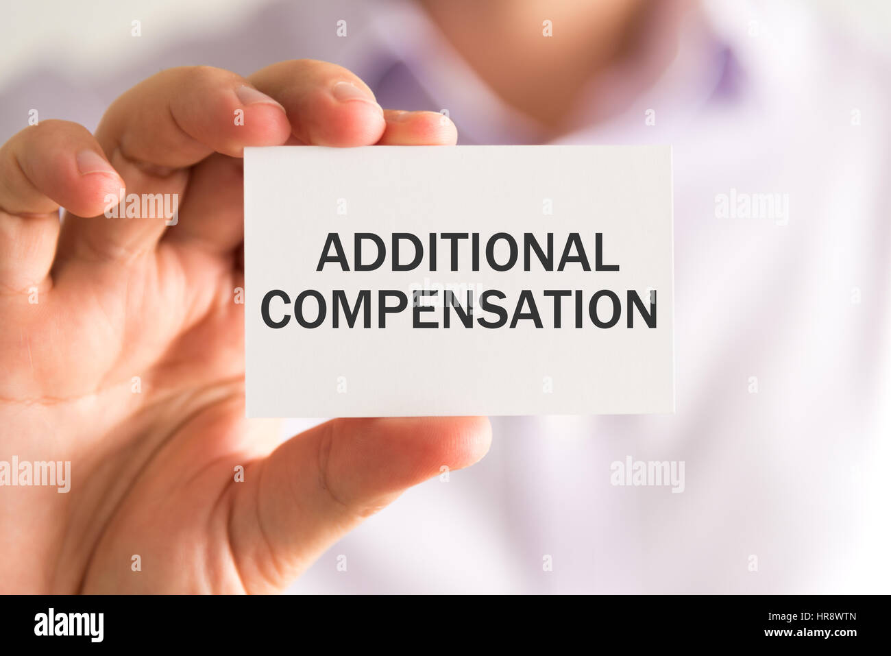 Closeup on businessman holding a card with ADDITIONAL COMPENSATION ...