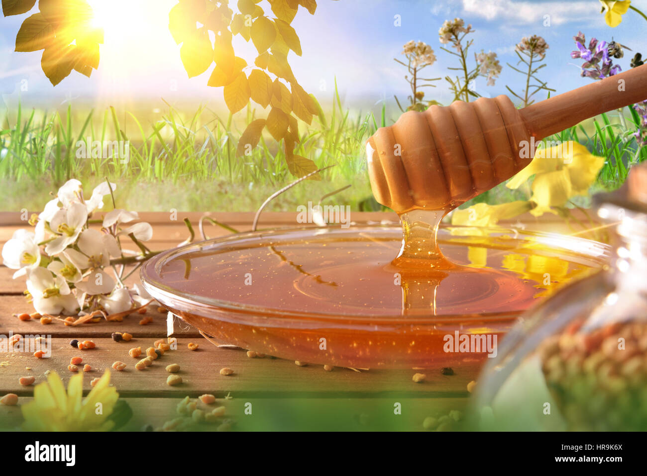 Honey falling into a glass dish on a wooden table with flowers and bee ...
