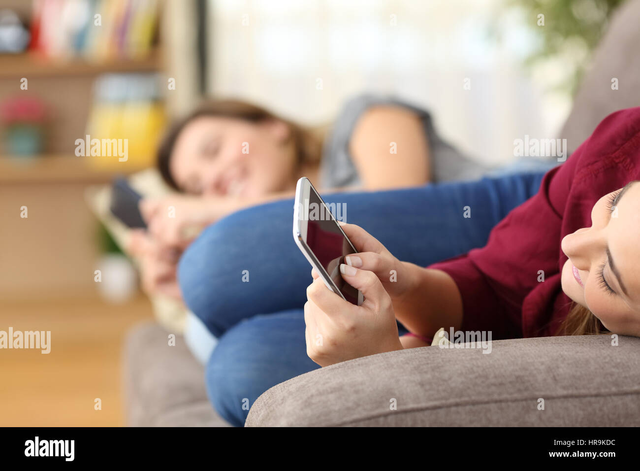 Two roommates using everyone their smart phones lying on a sofa in the ...