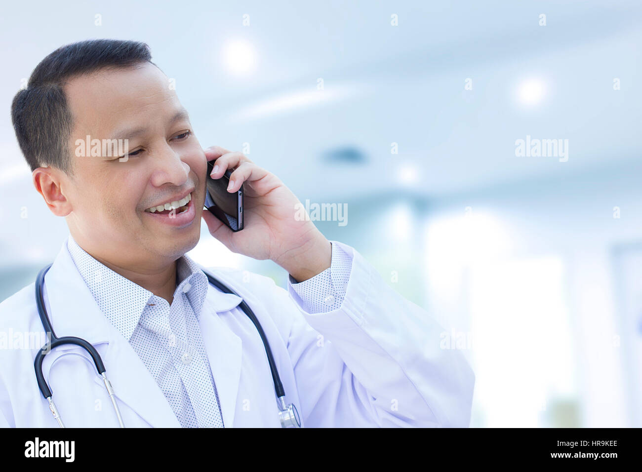 Asian male doctor using a mobile phone with a happy smile on blurry ...