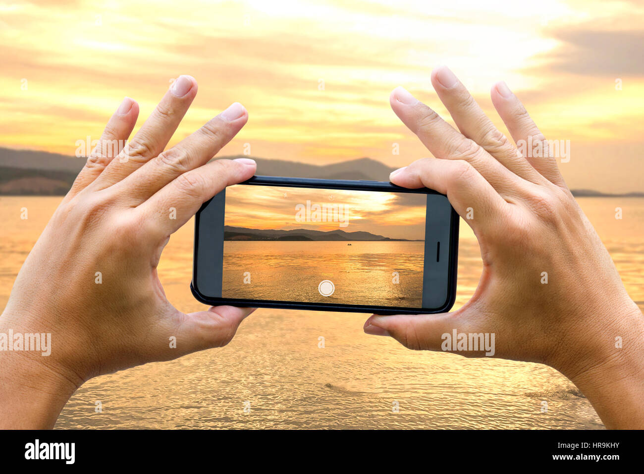 Two hands holding smart phone taking a photograph of sunset at Koh ...