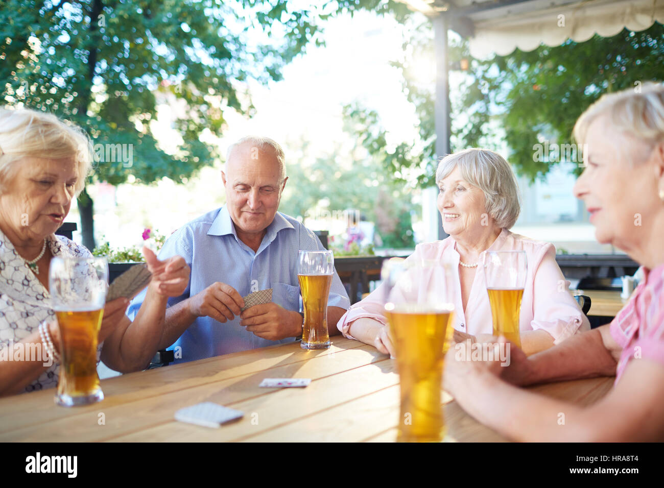 Cheerful seniors sitting in pub, drinking beer from glasses and playing ...