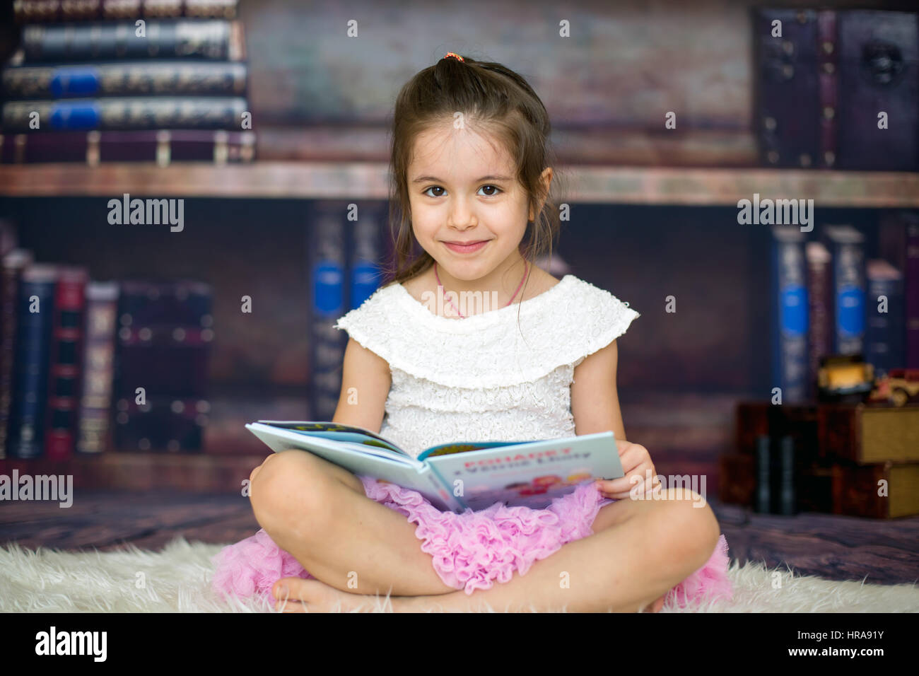 Sweet little girl, reading a book at home in front of the library Stock ...