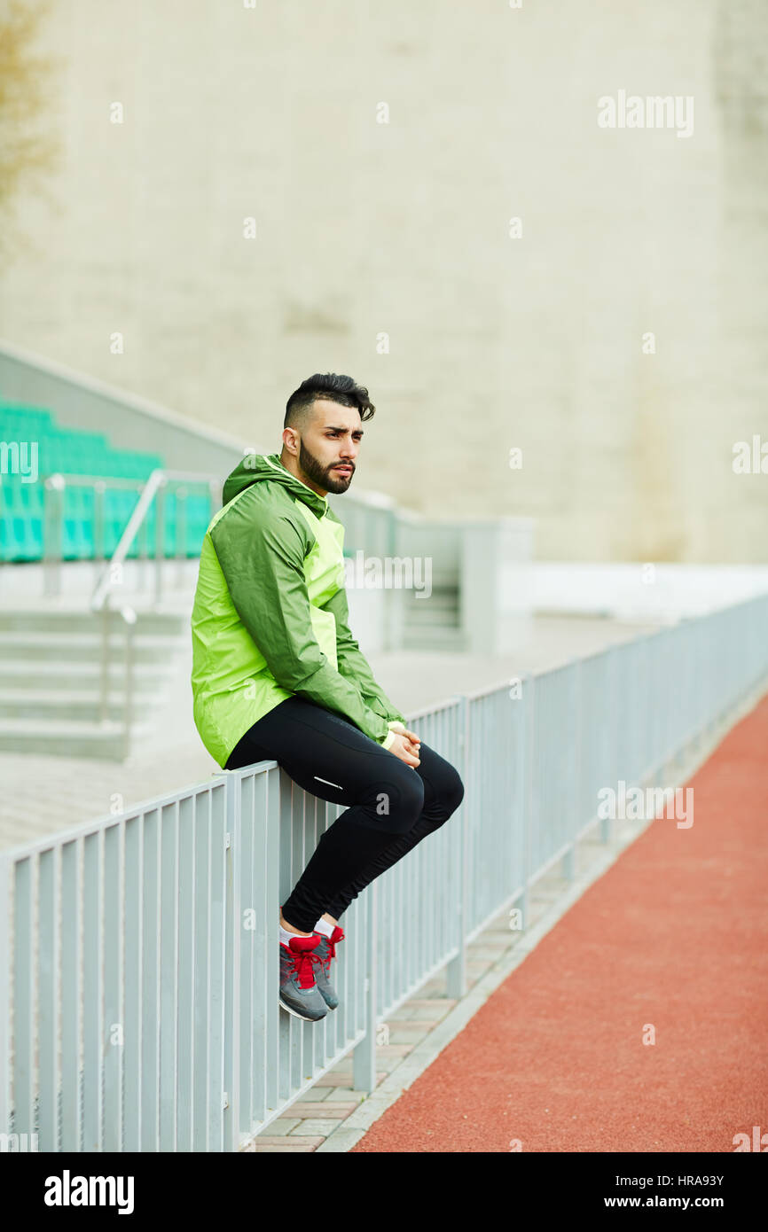 Young fashionable man sitting, resting on railings after running ...