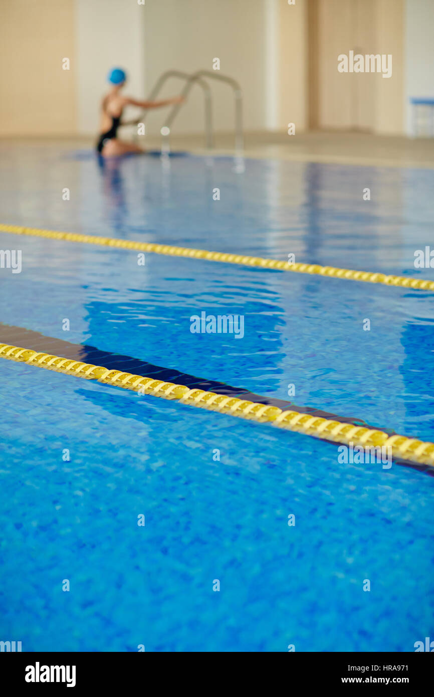 Clear blue water of indoor swimming pool with blurred shape of woman ...