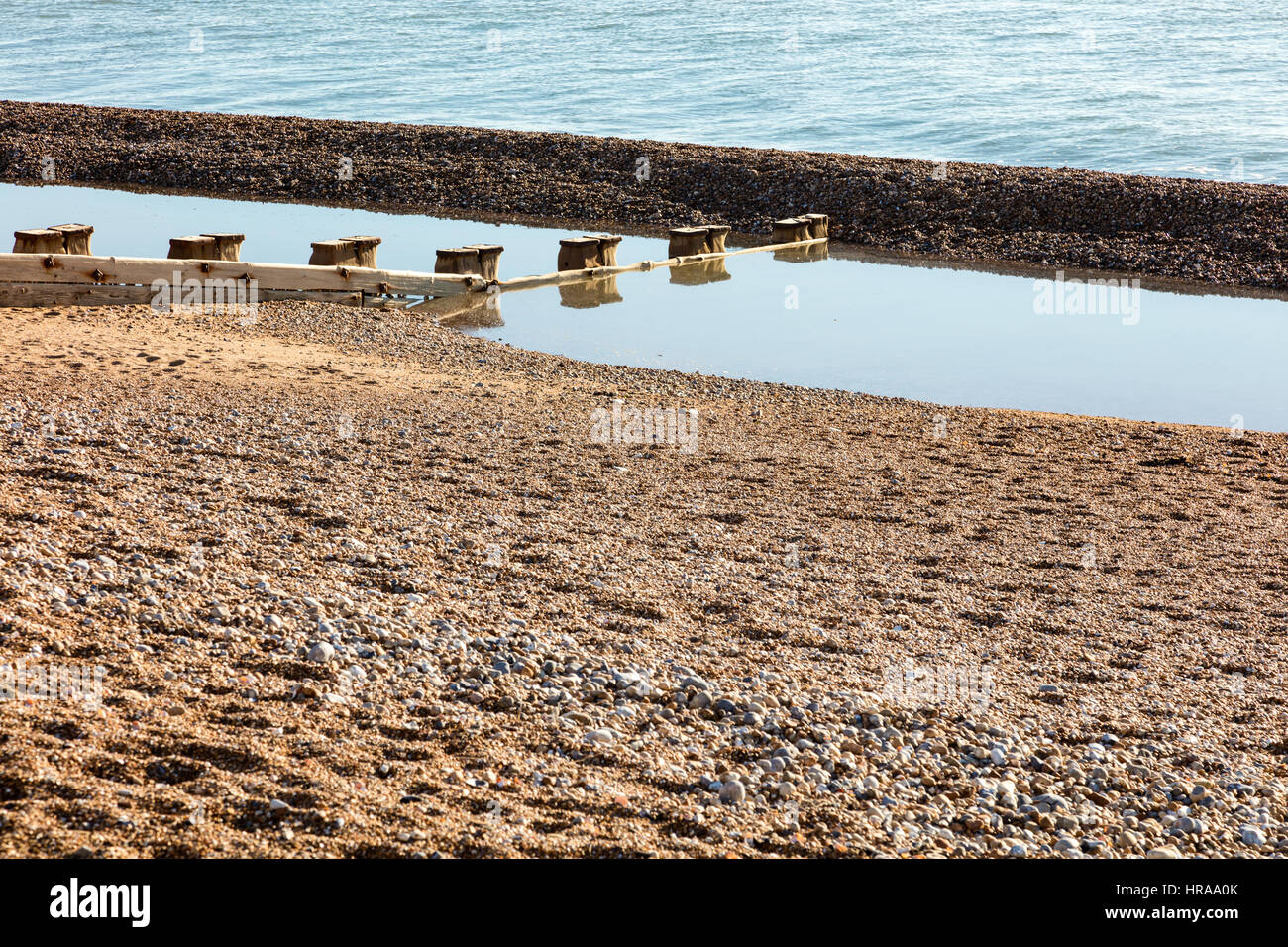 A shingle bank creates a pool of water on the beach at Bexhill on Sea ...