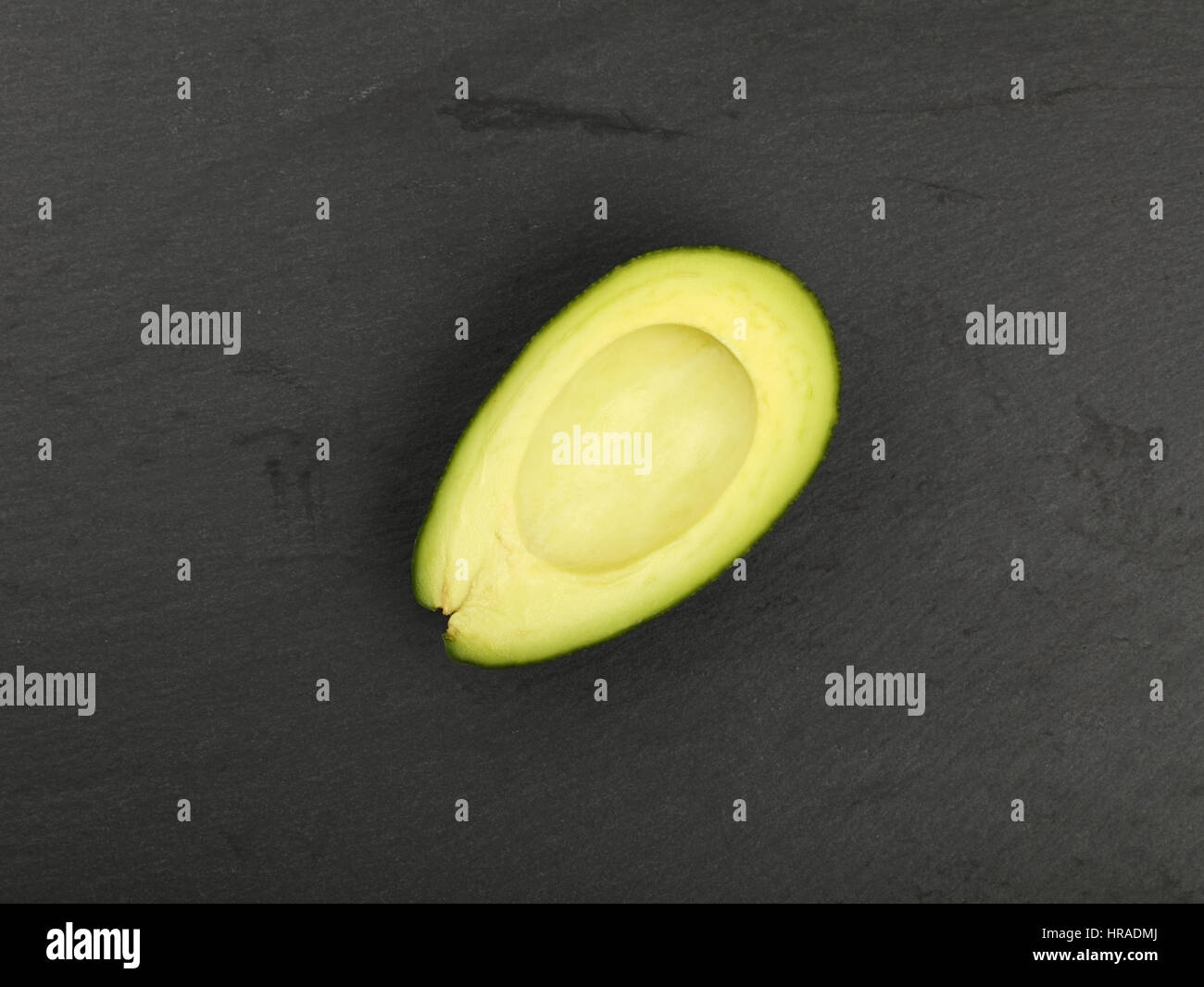 One fresh ripe green avocado half without pit stone on black slate ...