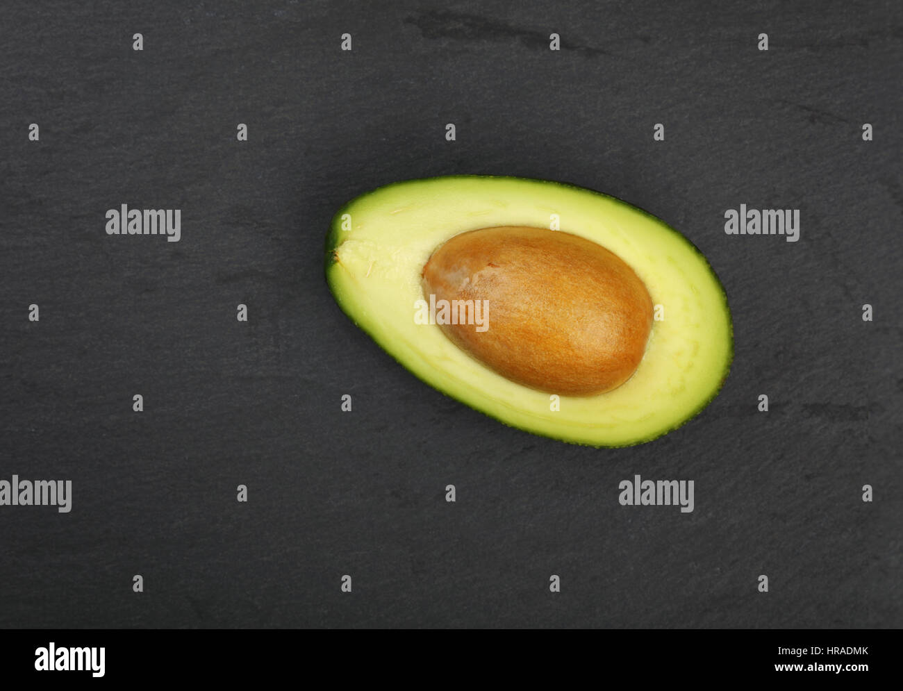 One fresh ripe green avocado half with pit stone on black slate board ...