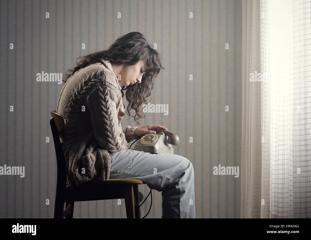 Sad woman sitting on a chair waiting for the phone call Stock Photo - Alamy