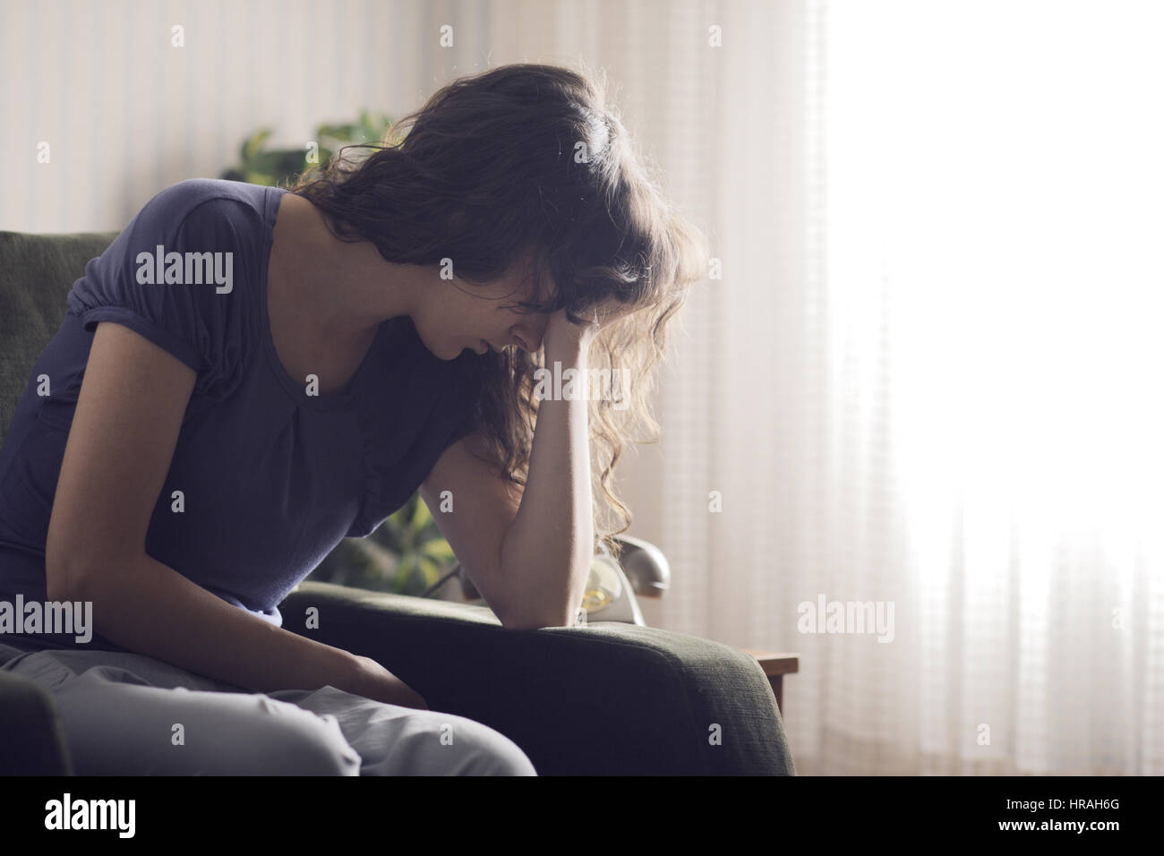 Depressed young woman sitting in chair at home Stock Photo - Alamy