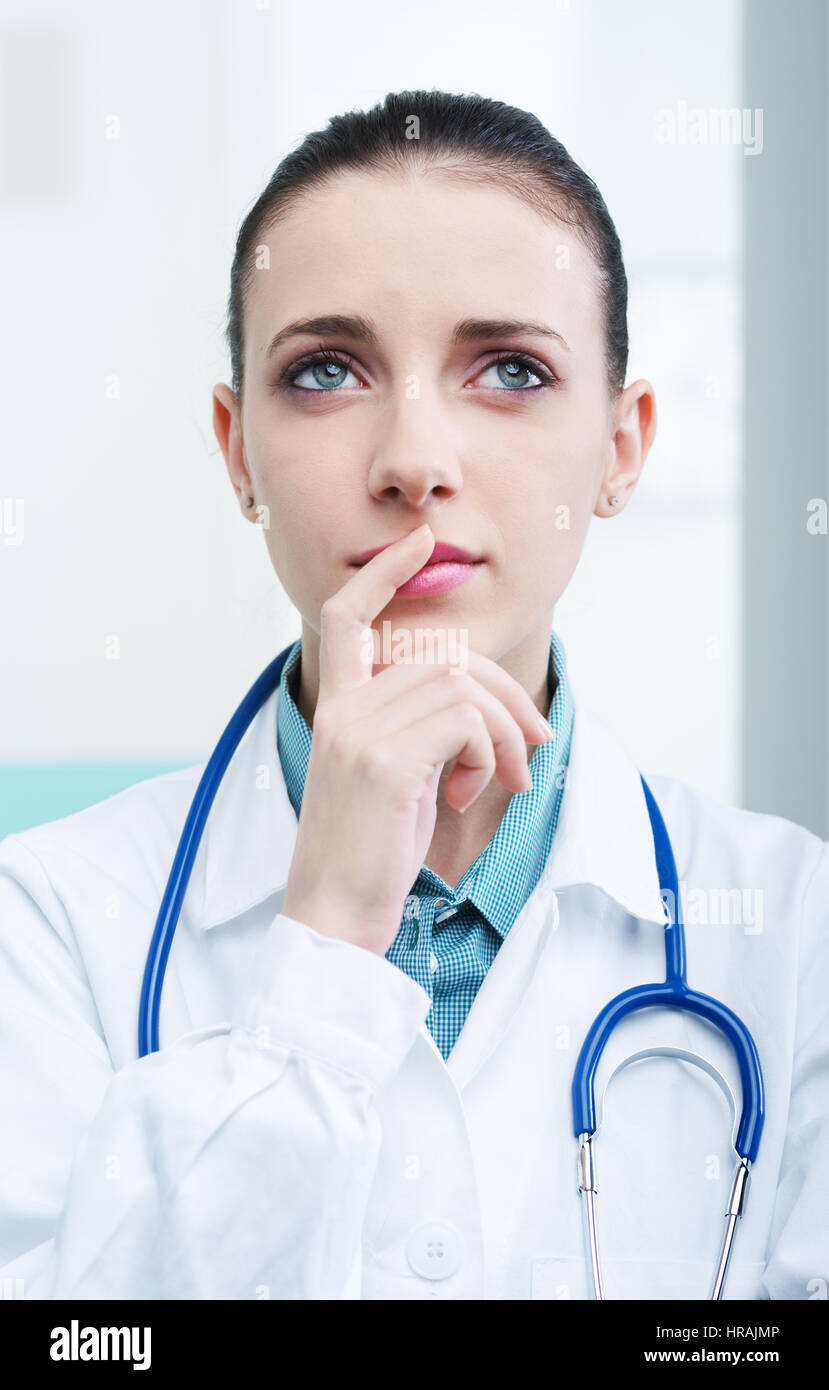 Portrait of a young female doctor thinking and looking up Stock Photo ...