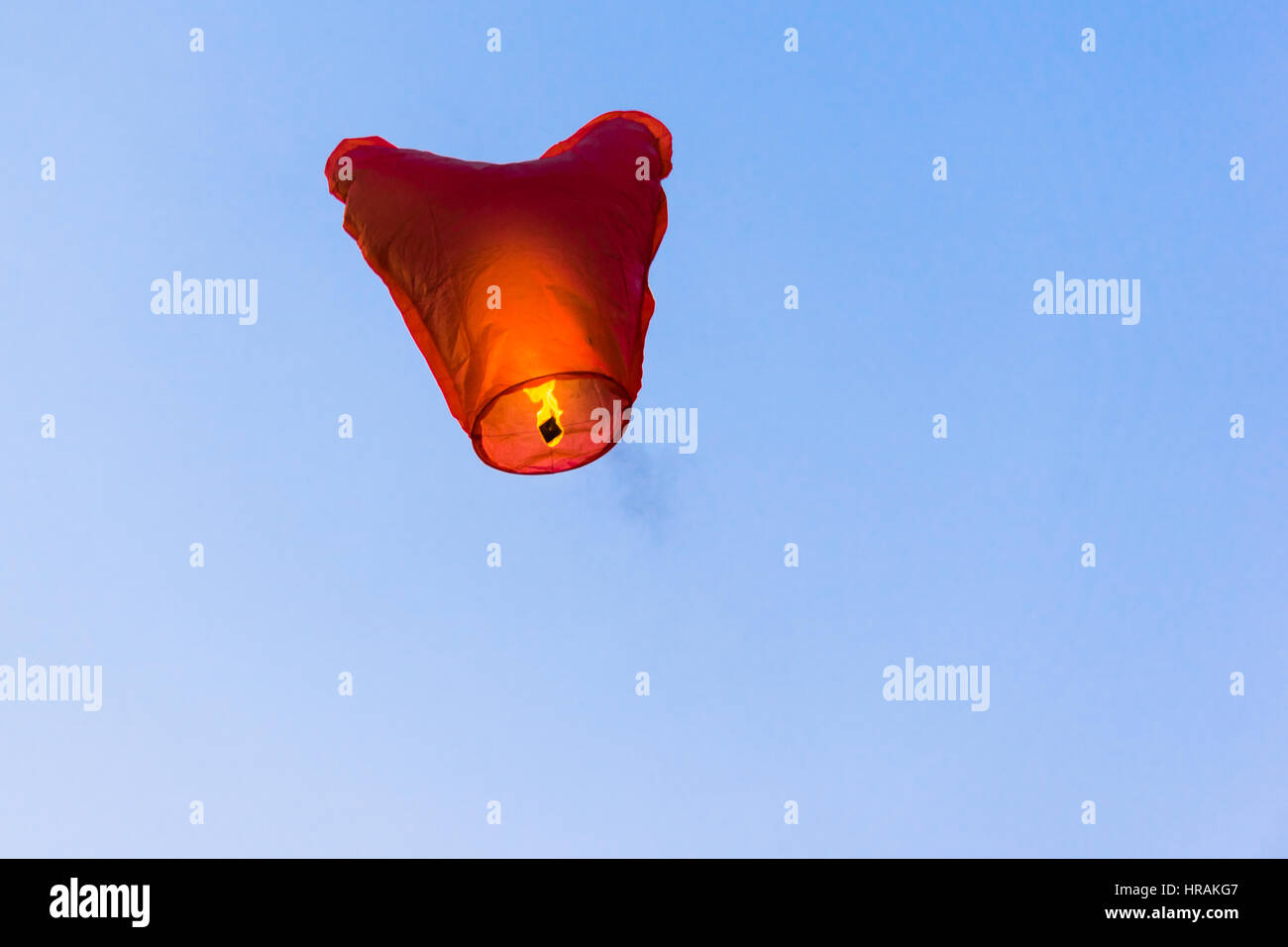 Red sky lantern flying against a blue sky with the flames showing ...